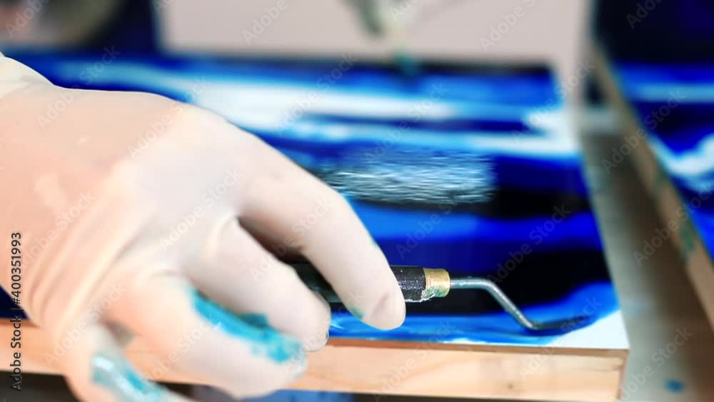 The artist smears paint around the edge of the painting with a tool ...