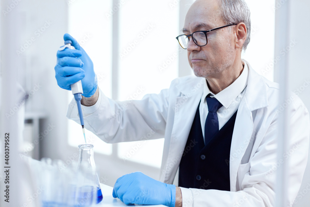 Elderly scientist doing pharmaceutical experiment using dropper pipette ...
