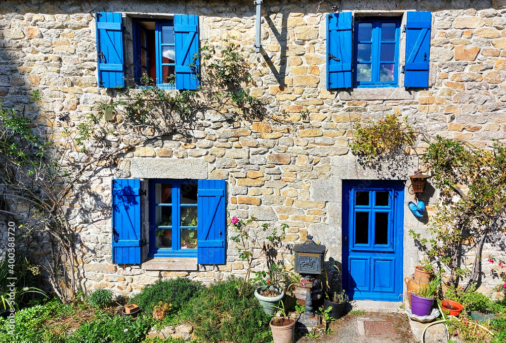 Façade d'une maison en pierre de granit, avec fenêtres et volets bleus ...