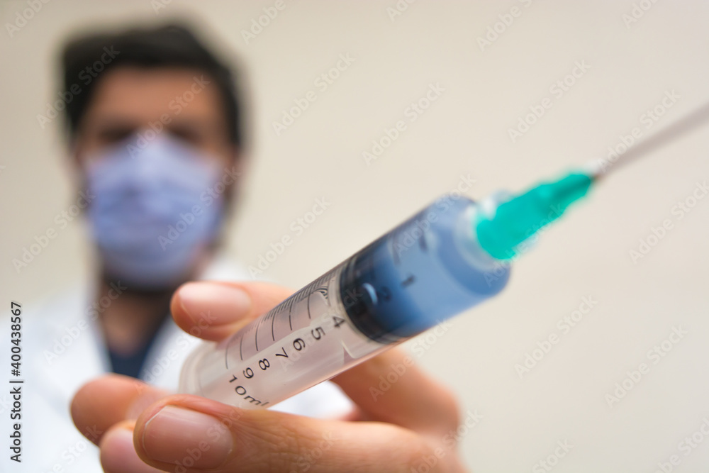 Disposable plastic syringe with blue liquid vaccine inside holding with ...