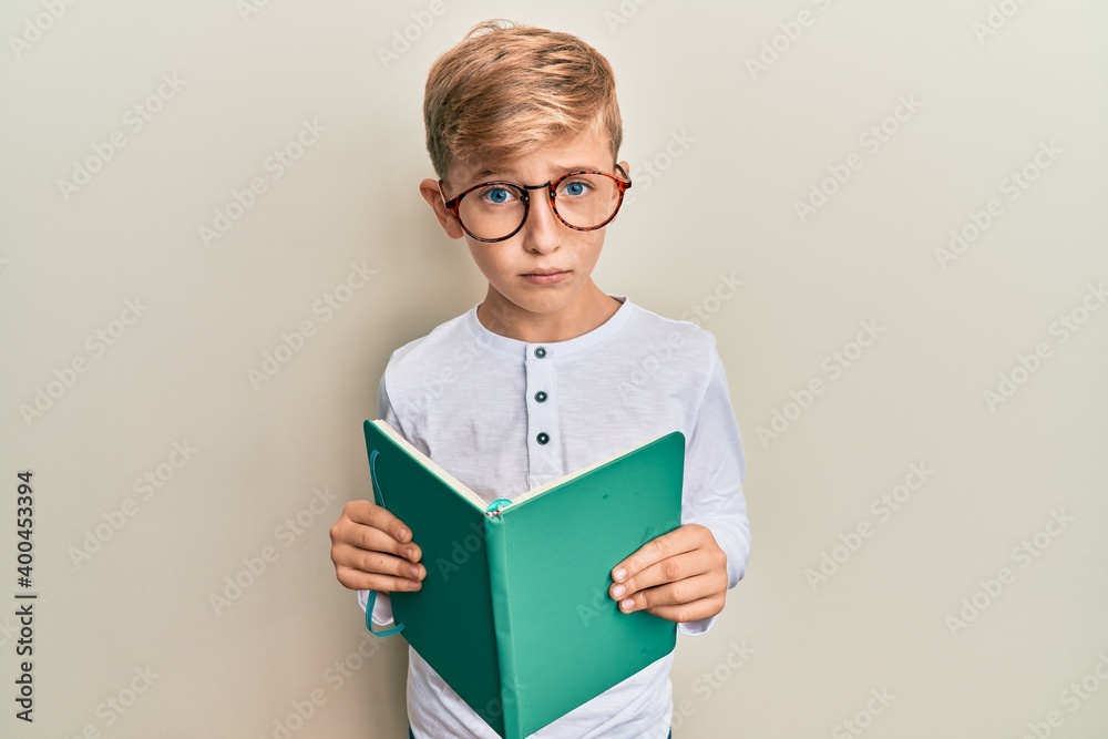 Little caucasian boy kid reading a book wearing glasses depressed and ...