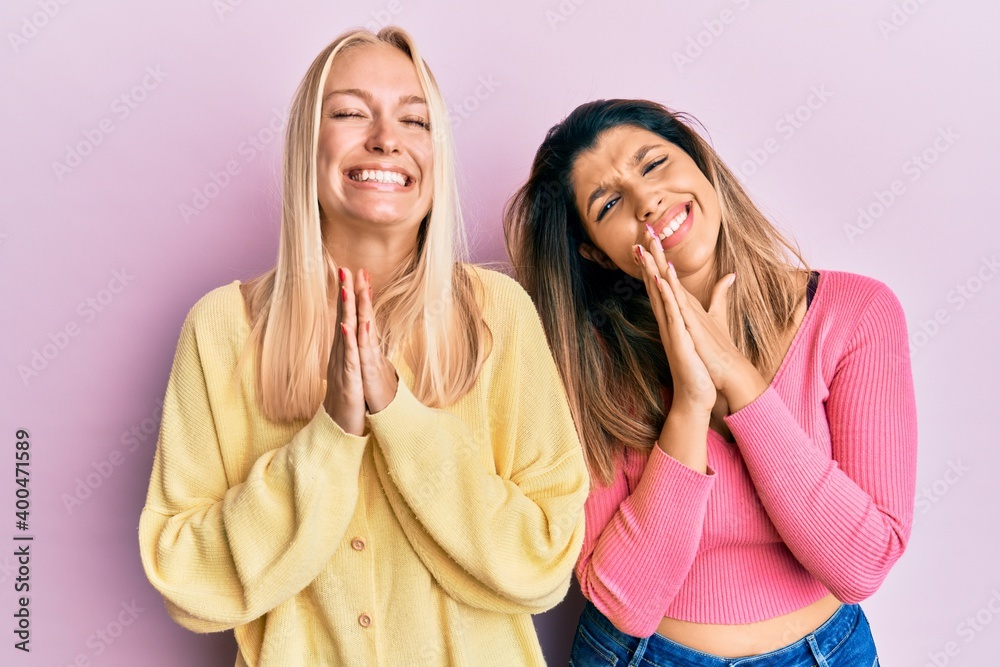 Two friends standing together over pink background begging and praying ...