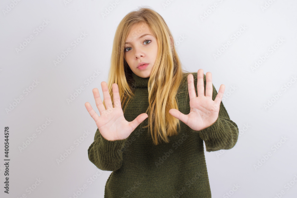 Caucasian kid girl wearing green knitted sweater against white wall ...