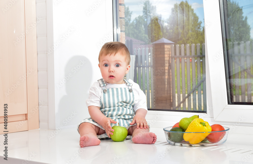Beautiful baby in the interior. Baby on the window playing with fruits ...