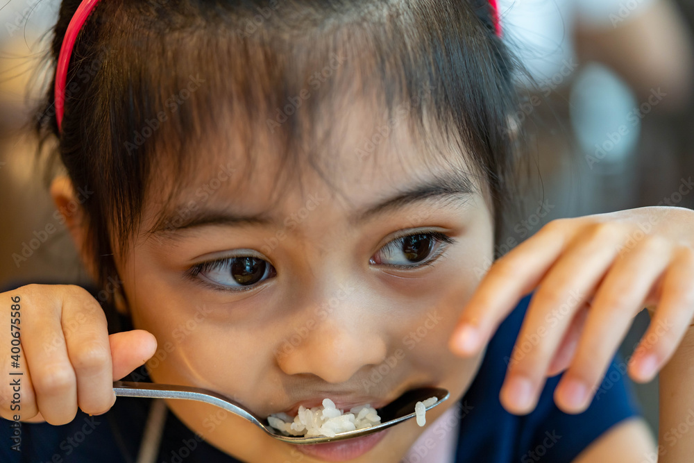 Female asian child while eating rice using spoon. Child enjoys eating ...