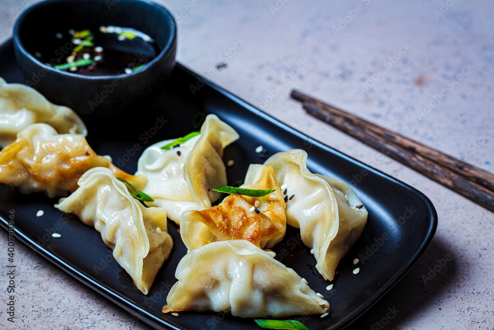 Fried gyoza dumplings with sauce and green onions on black plate, dark ...