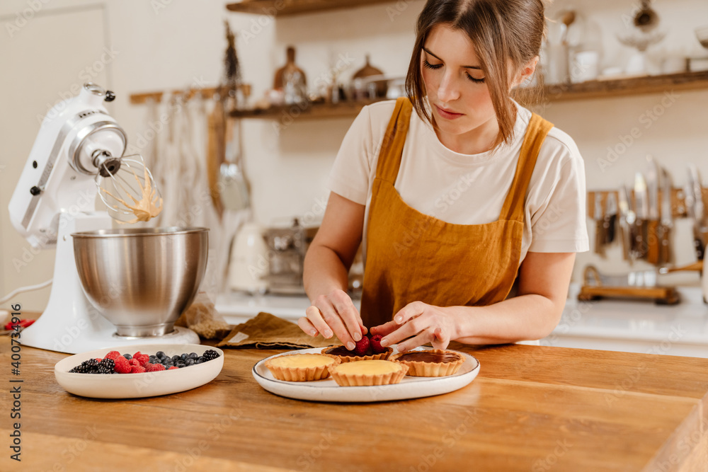 Beautiful concentrated pastry chef woman making tarts with berries ...