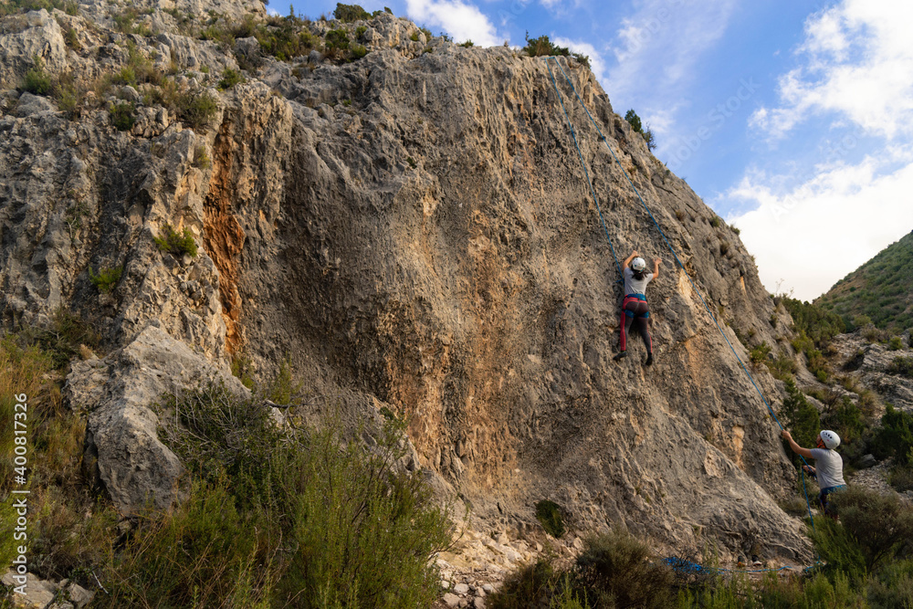 Young girl climber in the middle of a rock wall while her partner ...