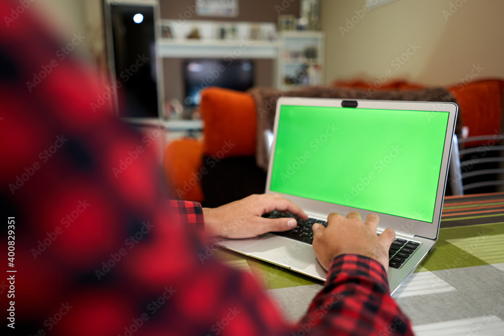 Teenager watching laptop with green screen. Man using keyboard and ...