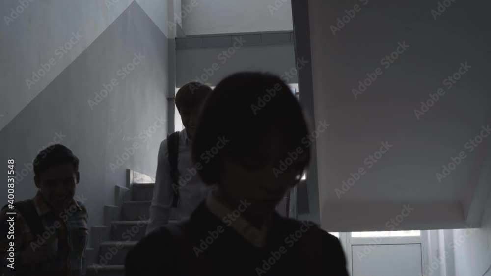 Portrait of frustrated teenage girl walking down stairs in public school with boys mocking at ...