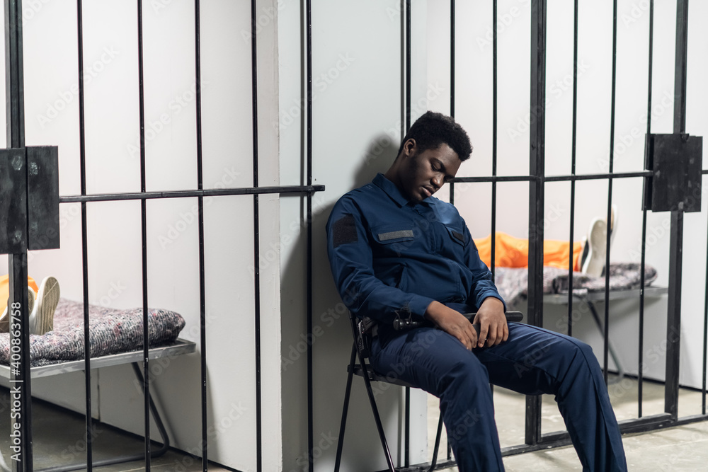 A strong black prison guard guards the cells with prisoners in the ...
