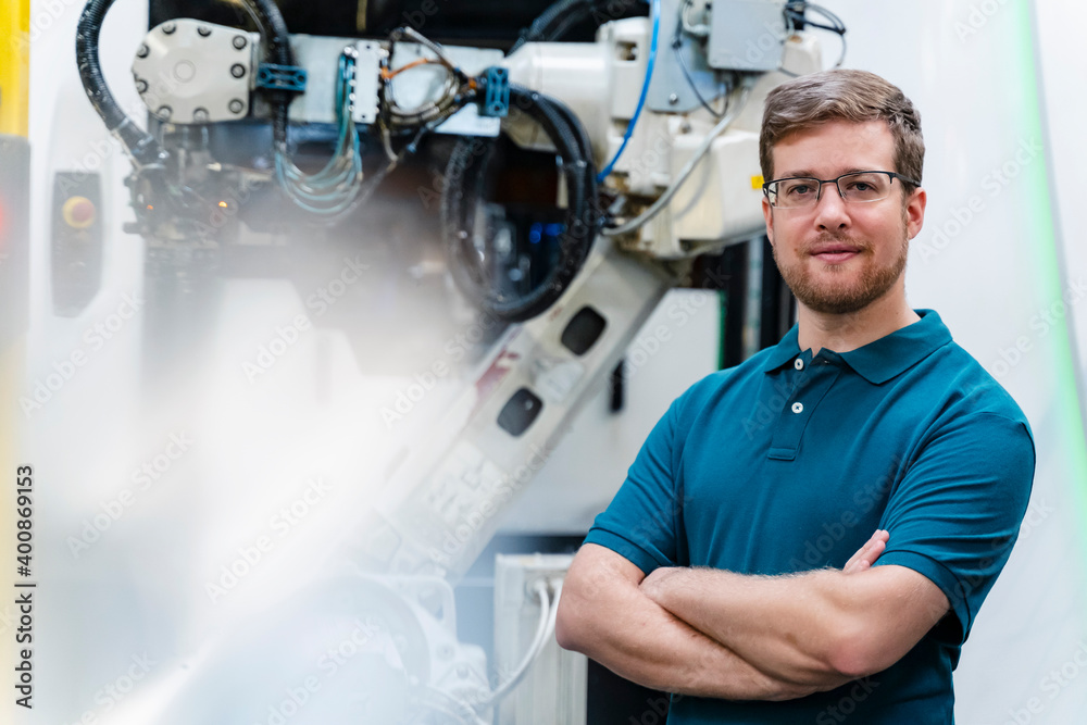 Confident male worker with arm crossed standing against industrial ...