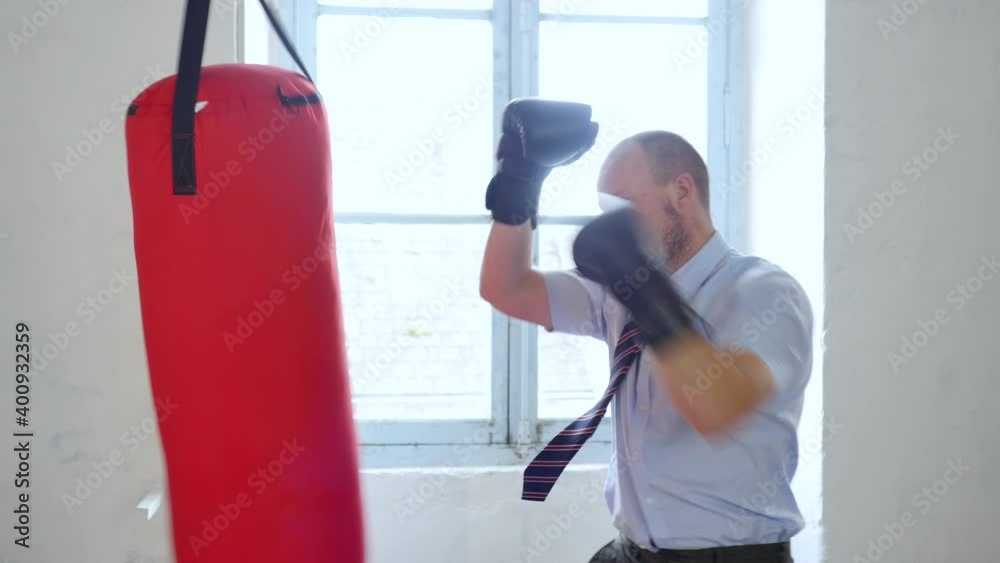 business man in shirt with tie and boxing gloves hitting punching ball ...