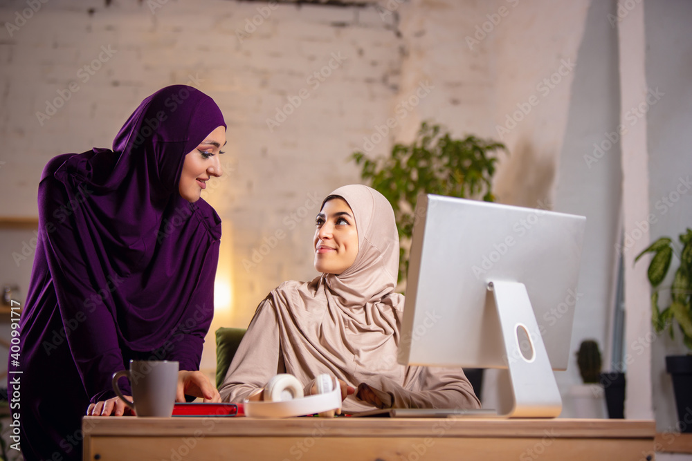 Disscussing. Happy and young two muslim women at home during lesson ...