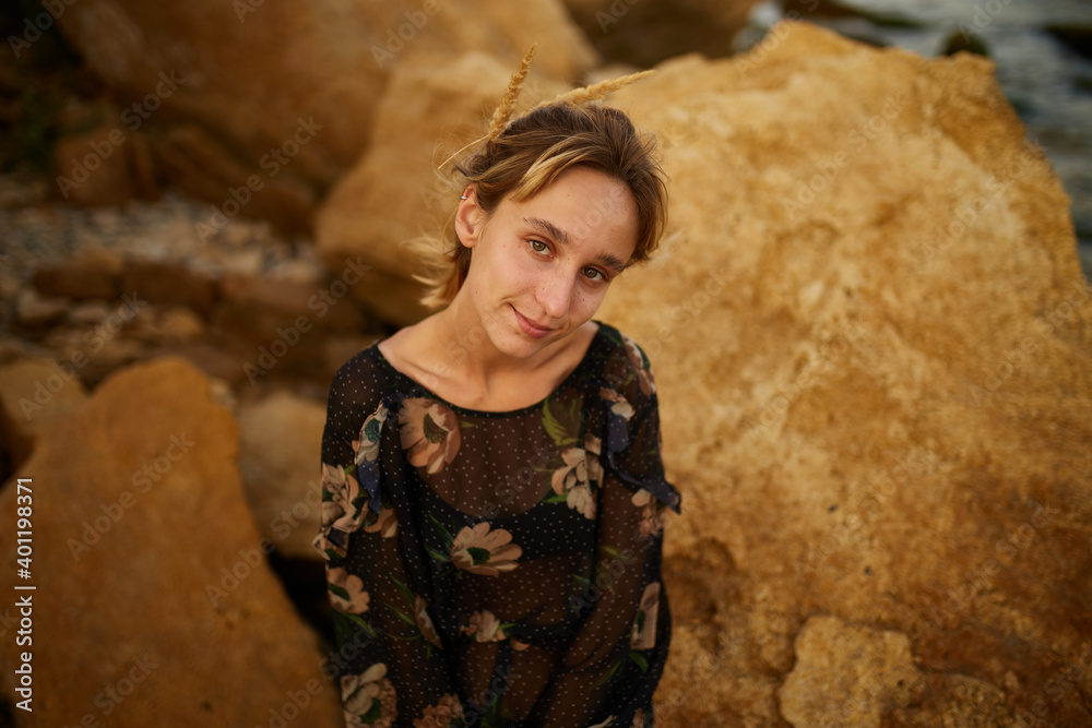 a beautiful girl sitting on the rocks by the sea in a dress. Portrait ...