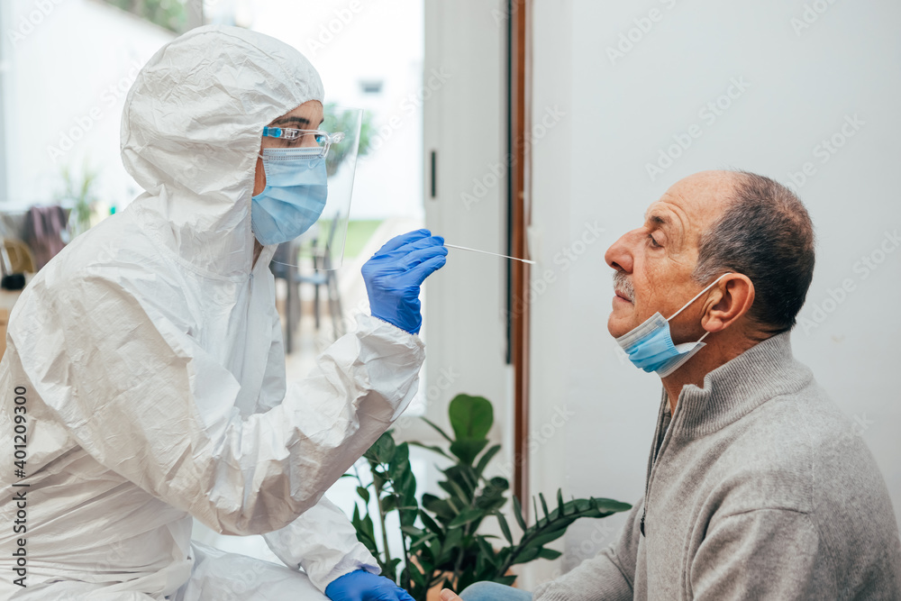 Health Professional in PPE suit and face shield introducing a nasal ...