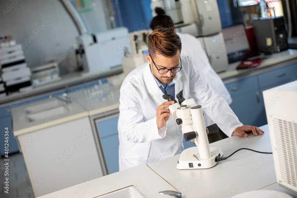 Young scientist in white lab coat working with binocular microscope in ...