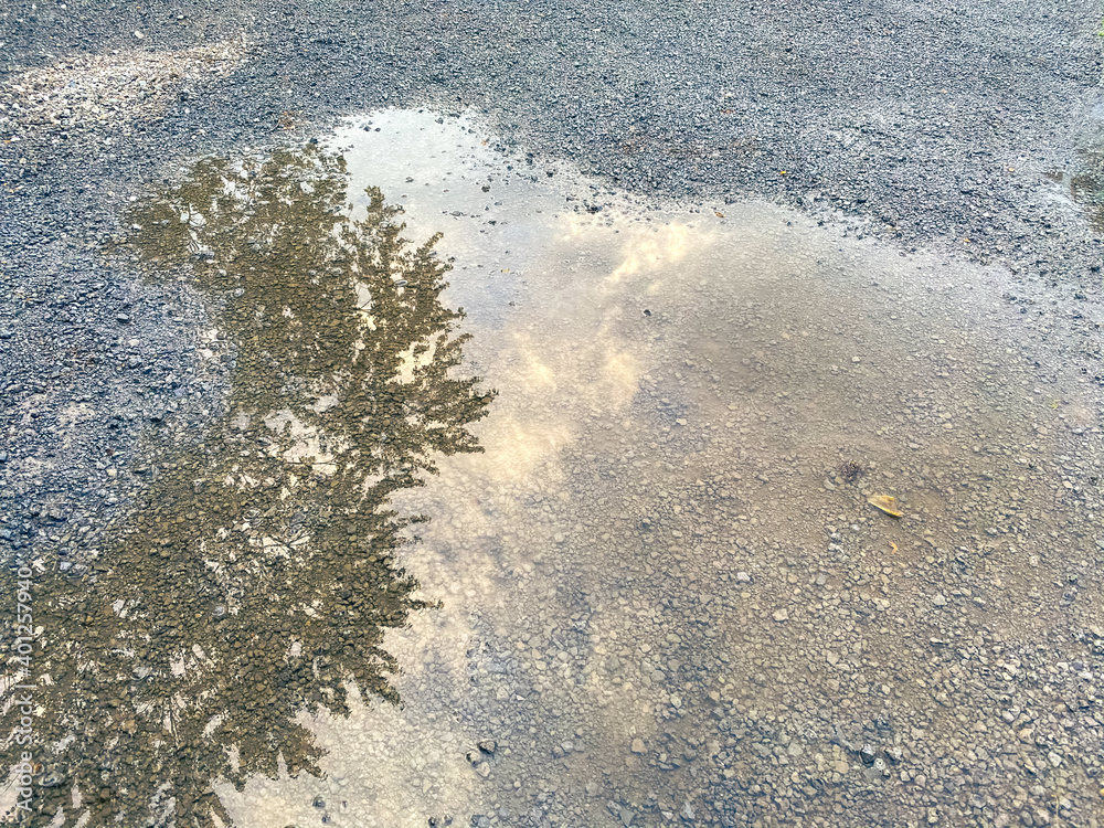 shallow rain puddle reflecting a cloudy sky with dirt and sand textures ...