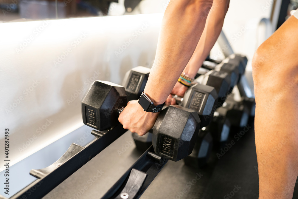 Anonymous person with smart watch taking heavy dumbbells from rack ...