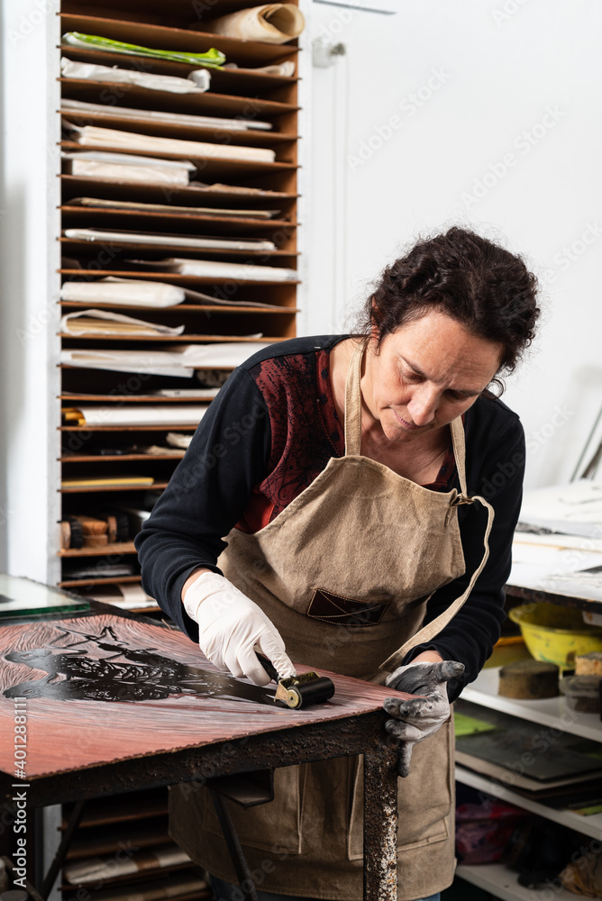 Mature female artist in apron and gloves covering engraved plate with ...