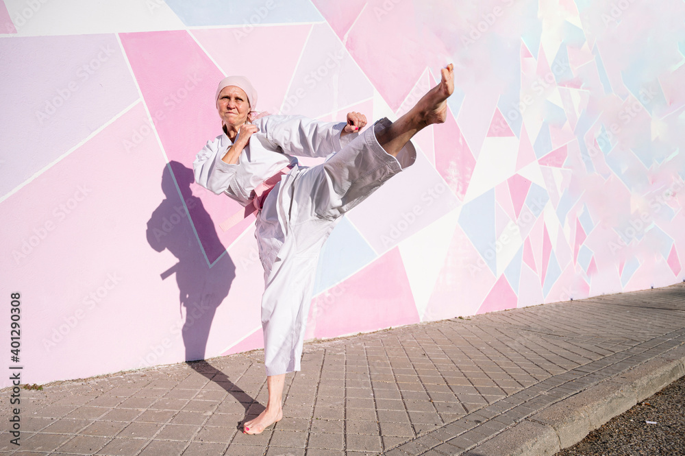 Determined mature barefooted woman in pink head cover and belt kicking ...