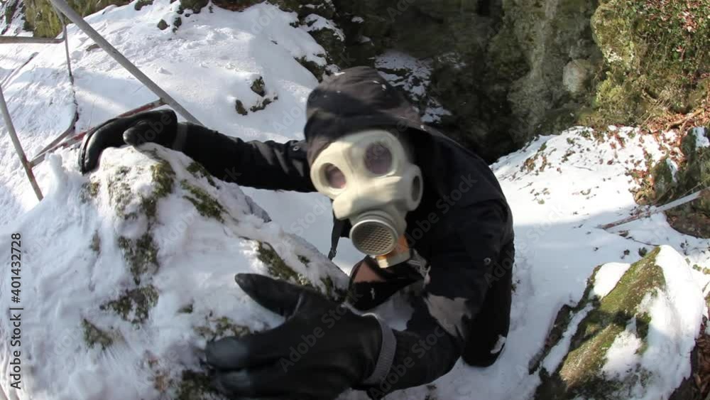 Strange man in gas mask acting hostile in front of a cave entrance ...