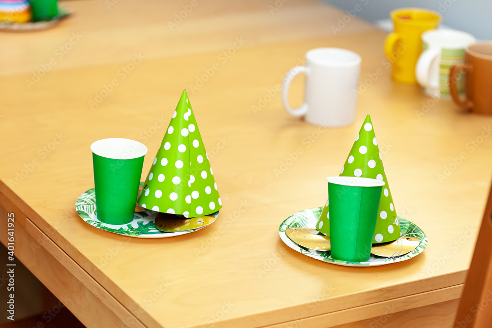 Party hats, paper plates, masks and green cups laying on the table ...