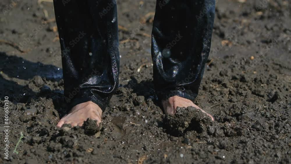 Male bare feet in black pants stand on wet ground, raindrops dripping ...
