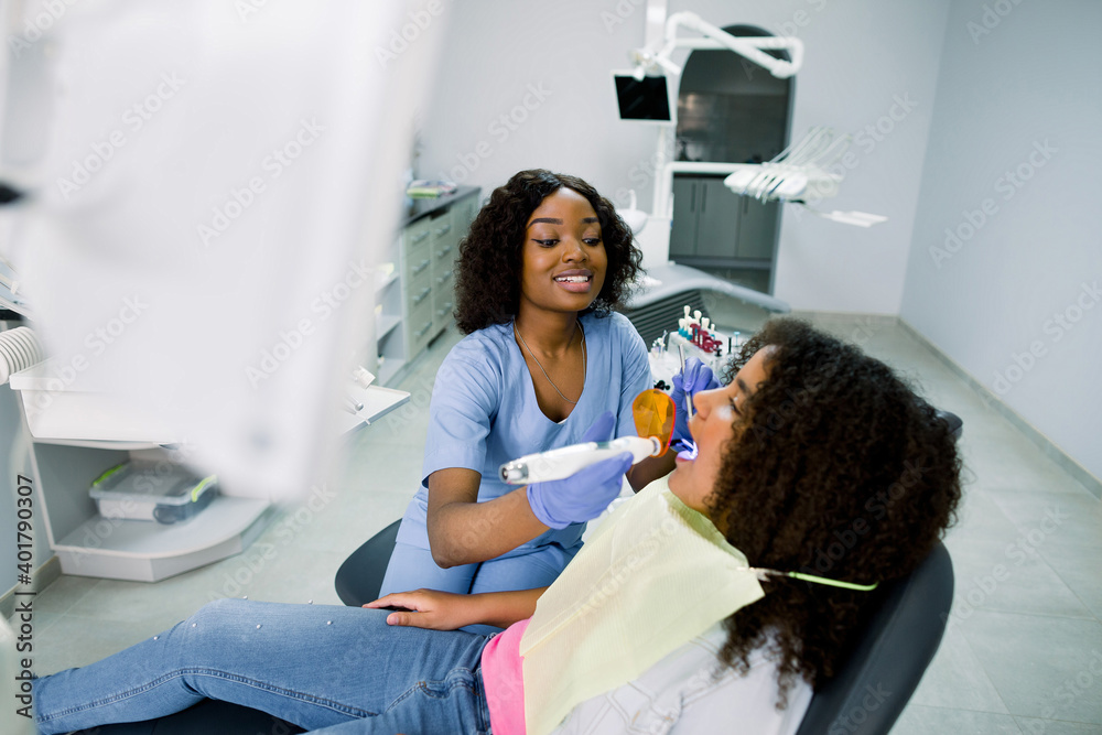 Smiling black woman dentist wearing blue uniform, providing tooth ...