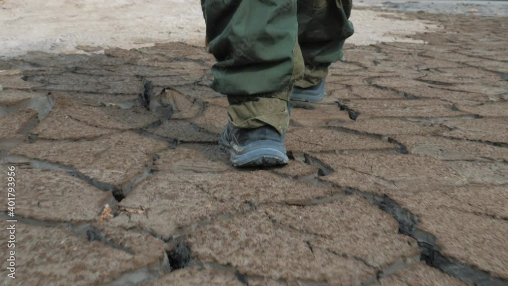 A man in boots walks on cracked soil during a drought and environmental ...
