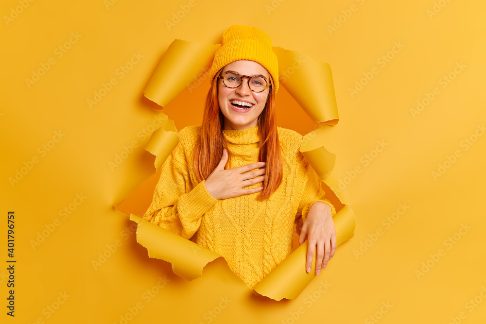 Positive ginger female model expresses sincere emotions keeps hand on ...
