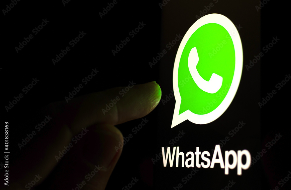 WhatsApp logo on the smartphone screen in a dark room and a finger ...