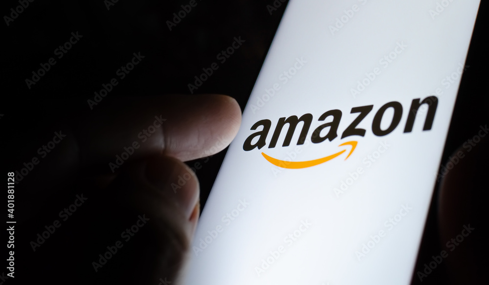 Amazon logo on a smartphone screen in a dark room and a finger pointing ...