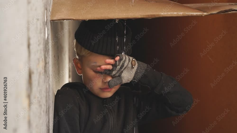 Poor orphan boy shelters from the rain under cardboard, crying ...