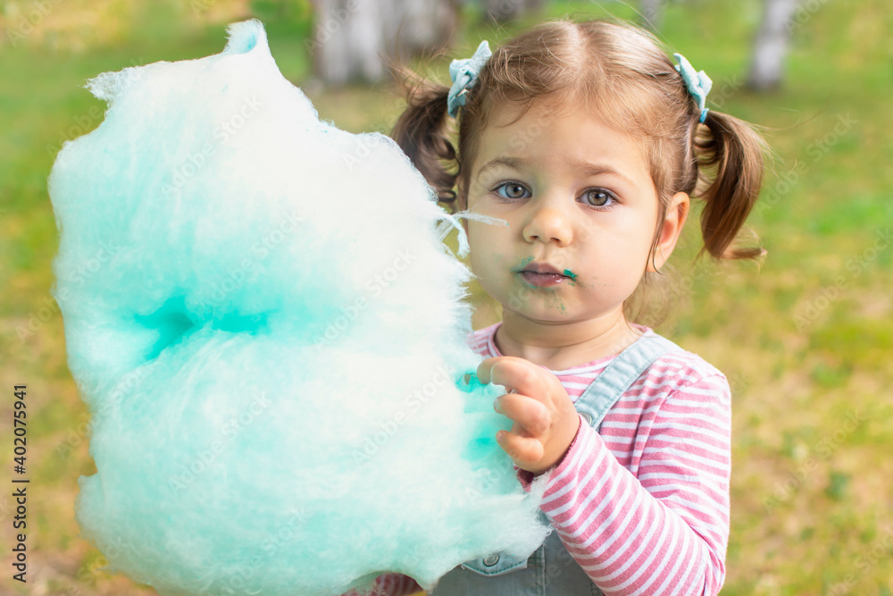 Cute adorable baby girl eating blue cotton candy outdoor. Funny child ...