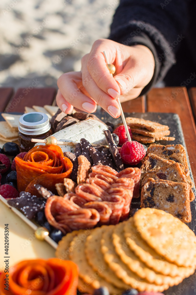 Woman's hand selecting a red raspberry from a grazing board filled with ...
