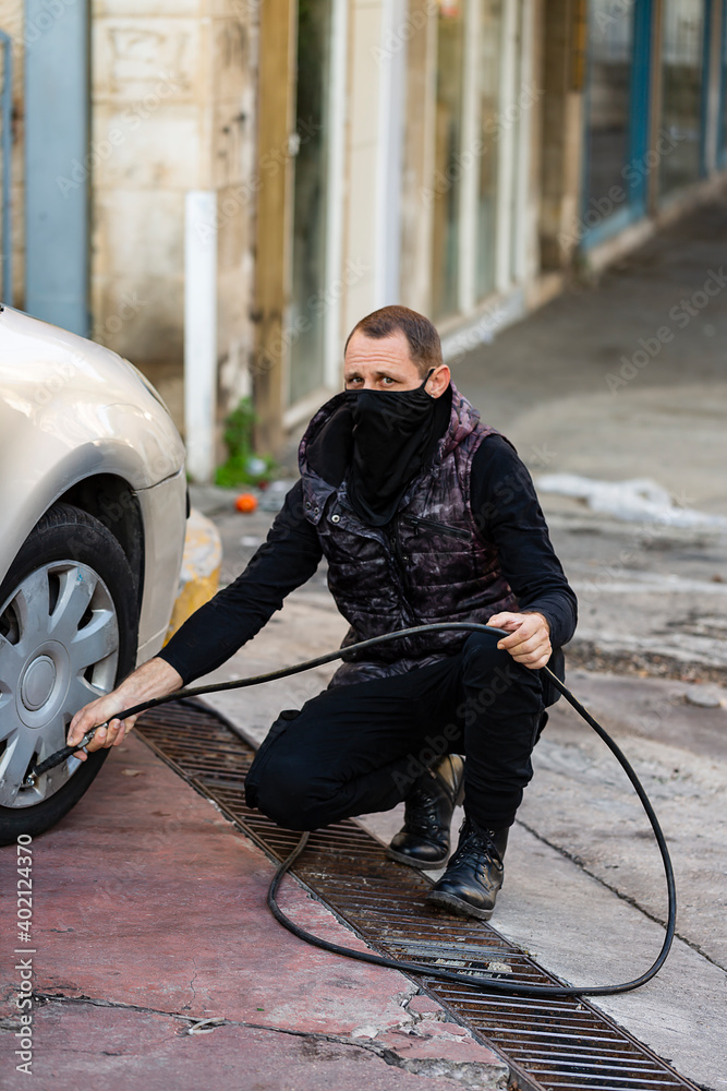 Masked car mechanic shakes a car wheel on the street in service station ...