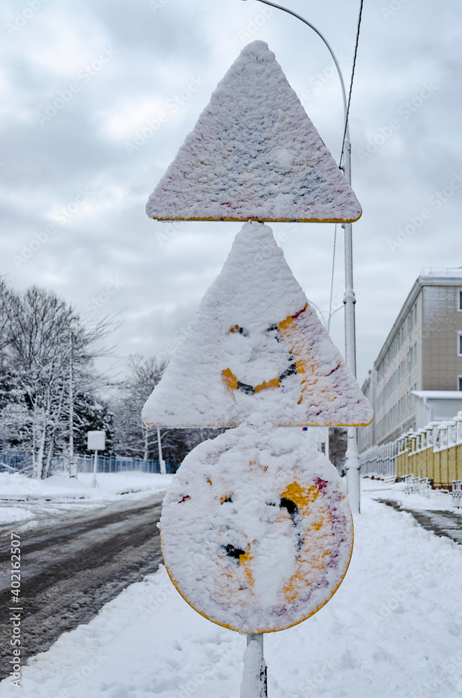 The road signs are covered with snow. A smiley face is drawn on the ...