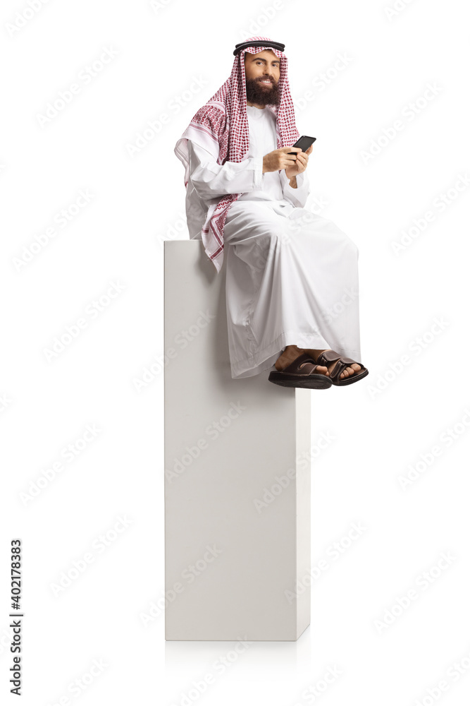 Saudi arab man holding a smartphone and sitting on a tall white column ...