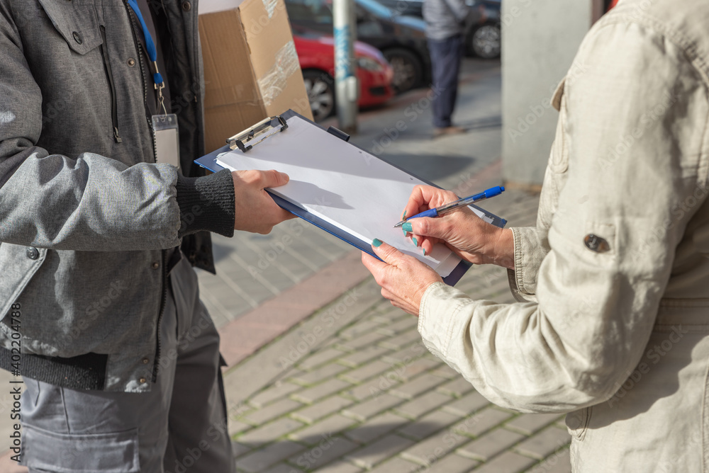 Courier delivering order to woman who signs for delivery of package, up ...