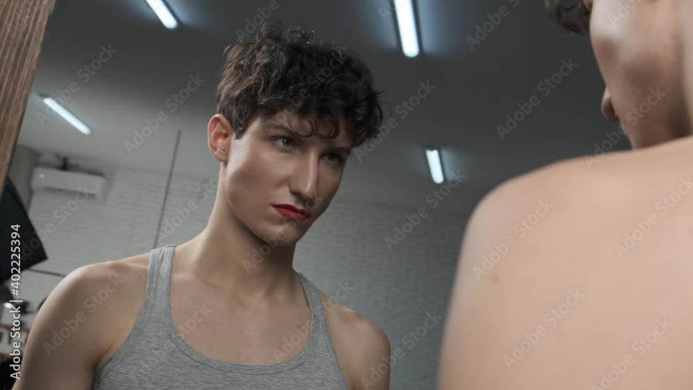 Confused and angry trans man stares in the mirror. Androgynous guy with ...