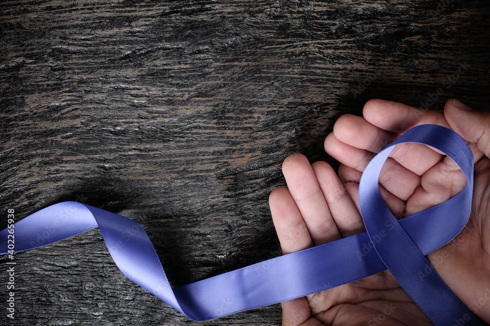 Top view of male hand holding periwinkle blue ribbon on wood background ...