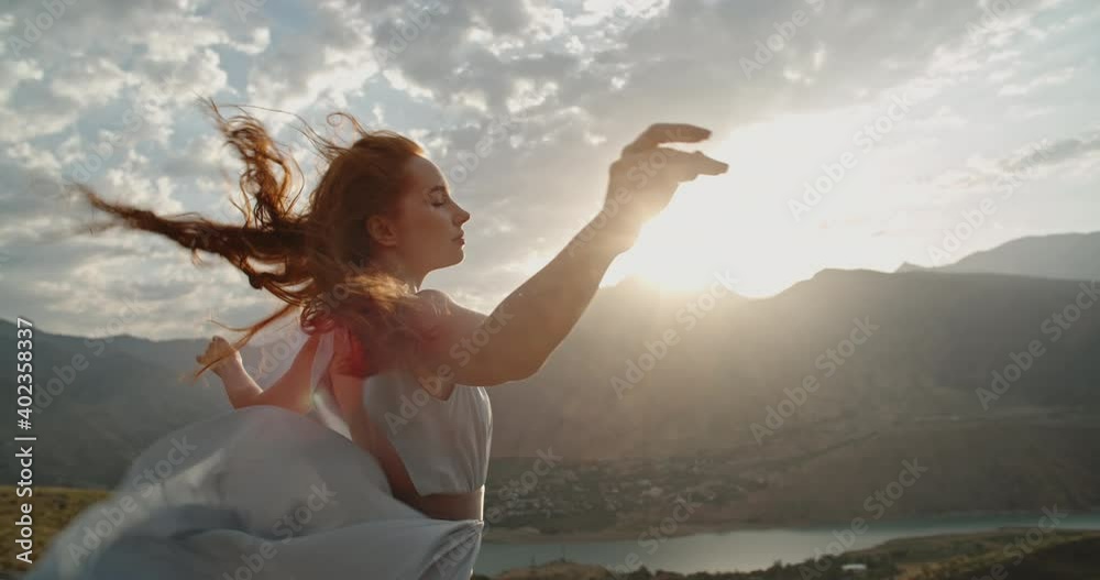Woman in white dress standing on top of a mountain with raised hands ...