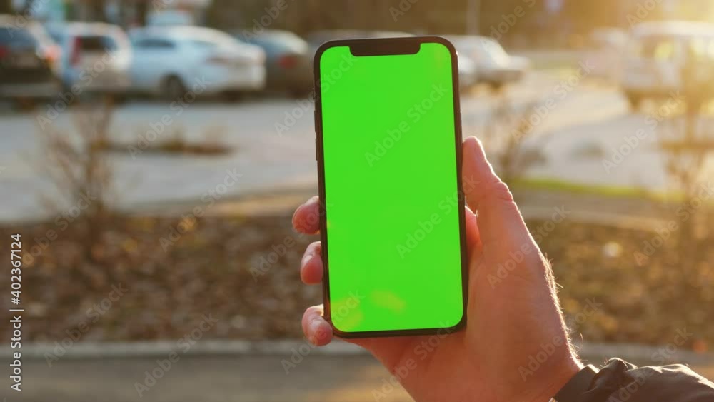 Man hand using touch phone with vertical green screen background sunlight road in city blurred ...
