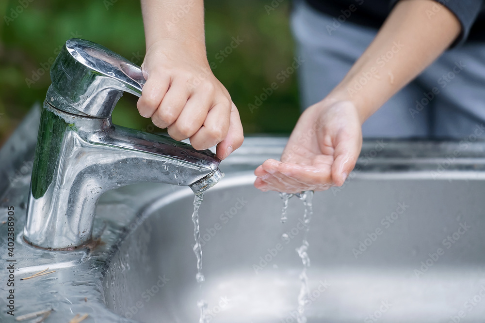 Baby try to turn off water faucet but water still leak. A child's hand turning off the tap. Save ...