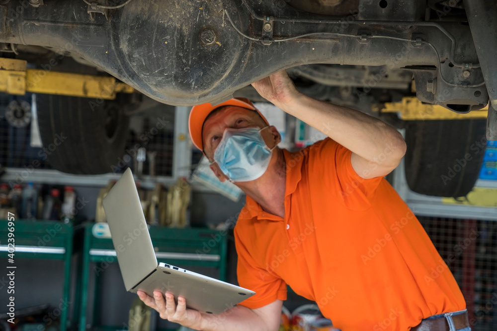 Senior car mechanic supervisor wearing mask and holding laptop to ...