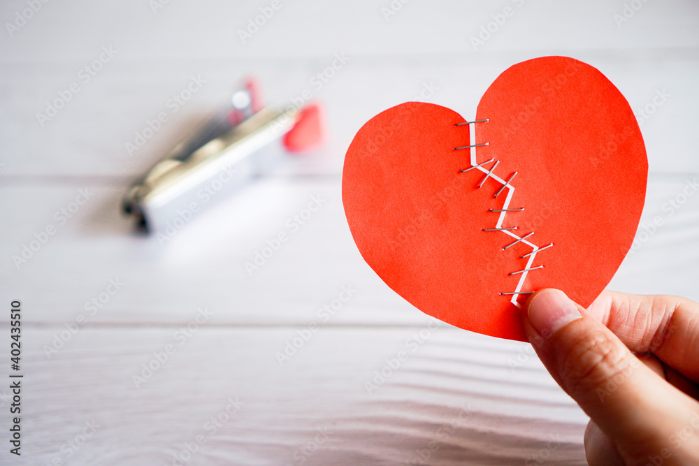 Hand of woman hold healed broken heart made from red paper with stapler ...