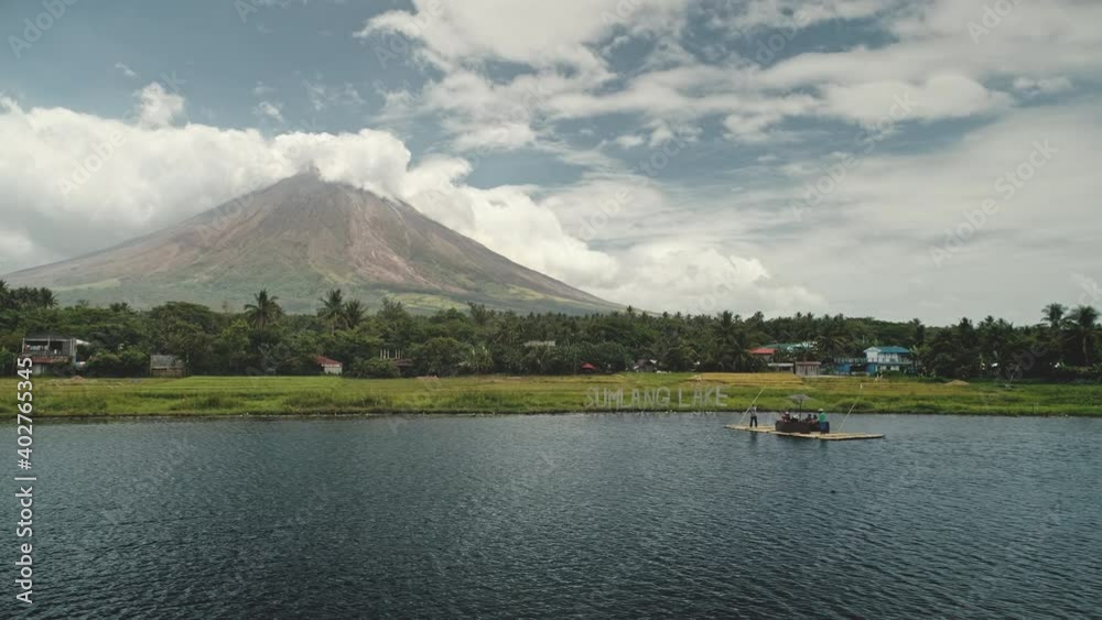 Mayon volcano at lake shore aerial. Tourist at boat sail to green grass ...