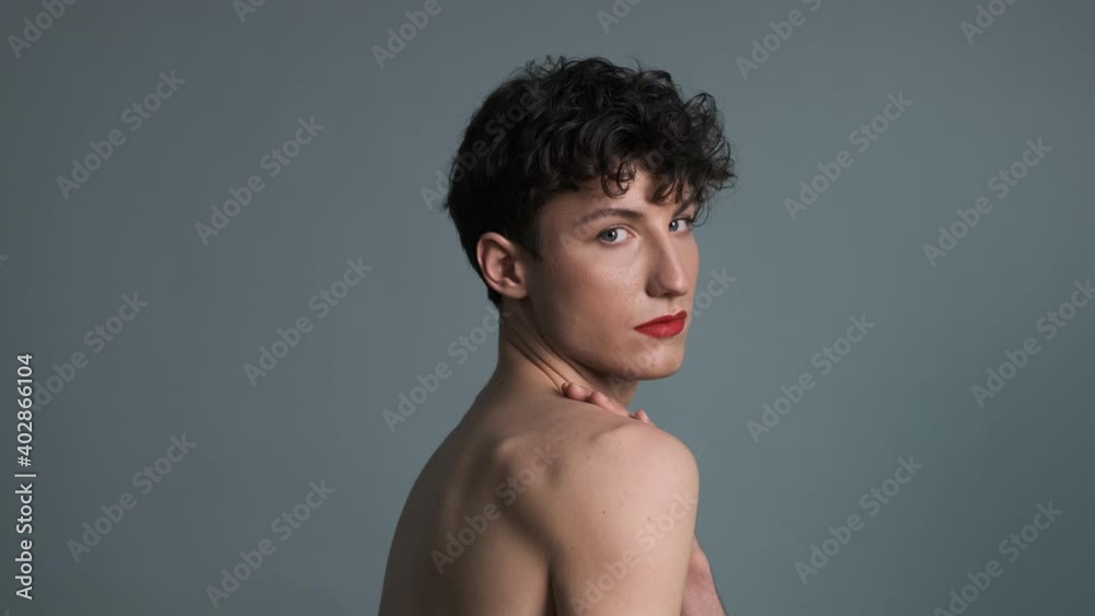 Portrait of a fashionable transgender with makeup posing on grey ...