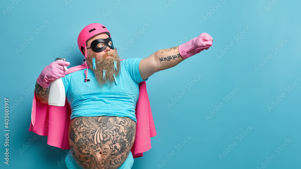 Serious bearded fatso man dressed in superhero costume holds detergent ...